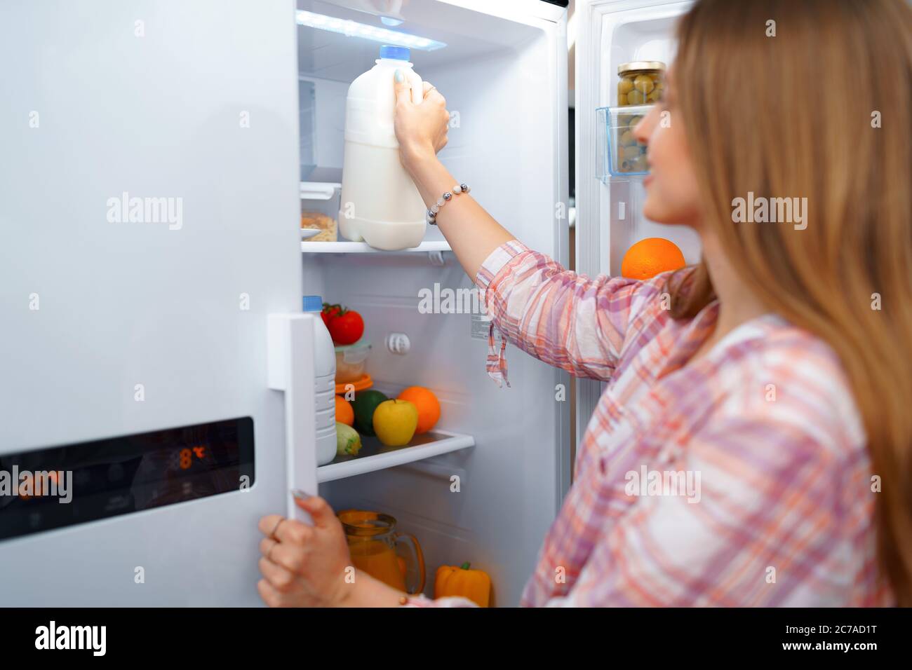Portrait of a young blonde woman taking food from her fridge Stock ...