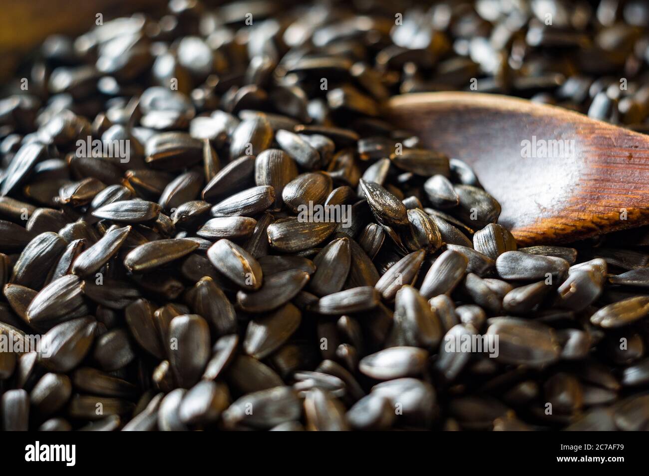 Fried sunflower black seeds with a wooden spoon in a pan, close-up ...