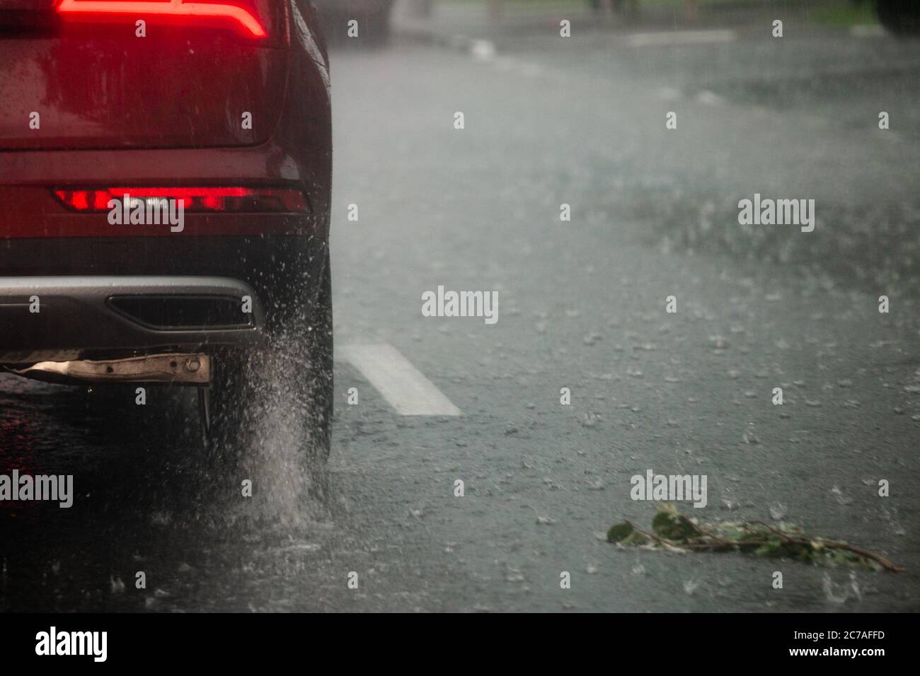 Rain water splash flow from wheels of red car moving fast in daylight ...