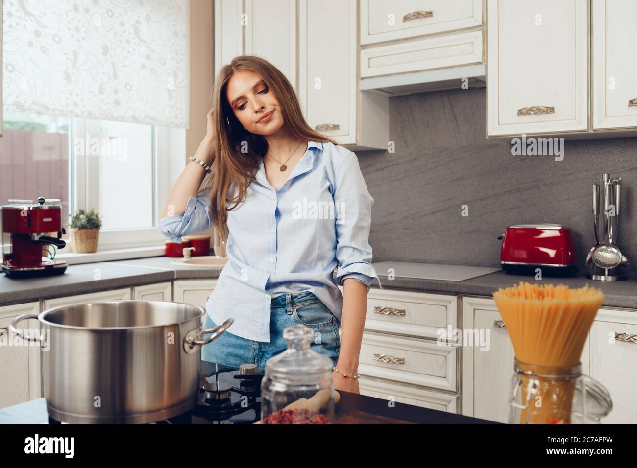 Pensive young woman standing in the kitchen and thinking of what to ...