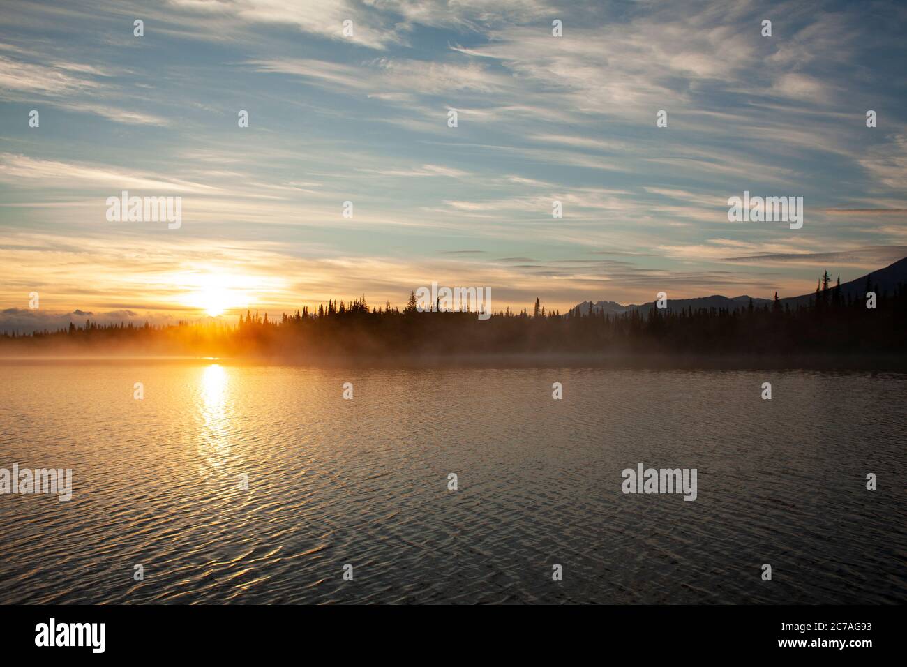 Golden sunset over an Alaskan lake, with mountain silhouettes and soft ...