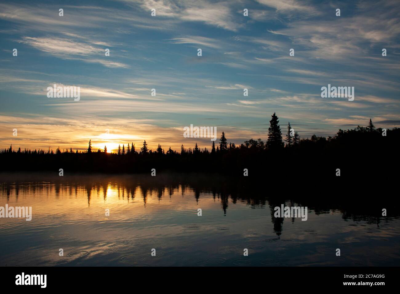 Golden sunset over an Alaskan lake, with mountain silhouettes and soft ...