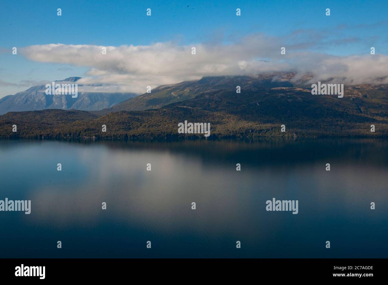 Calm waters of an Alaskan lake reflecting cloud-covered mountains ...