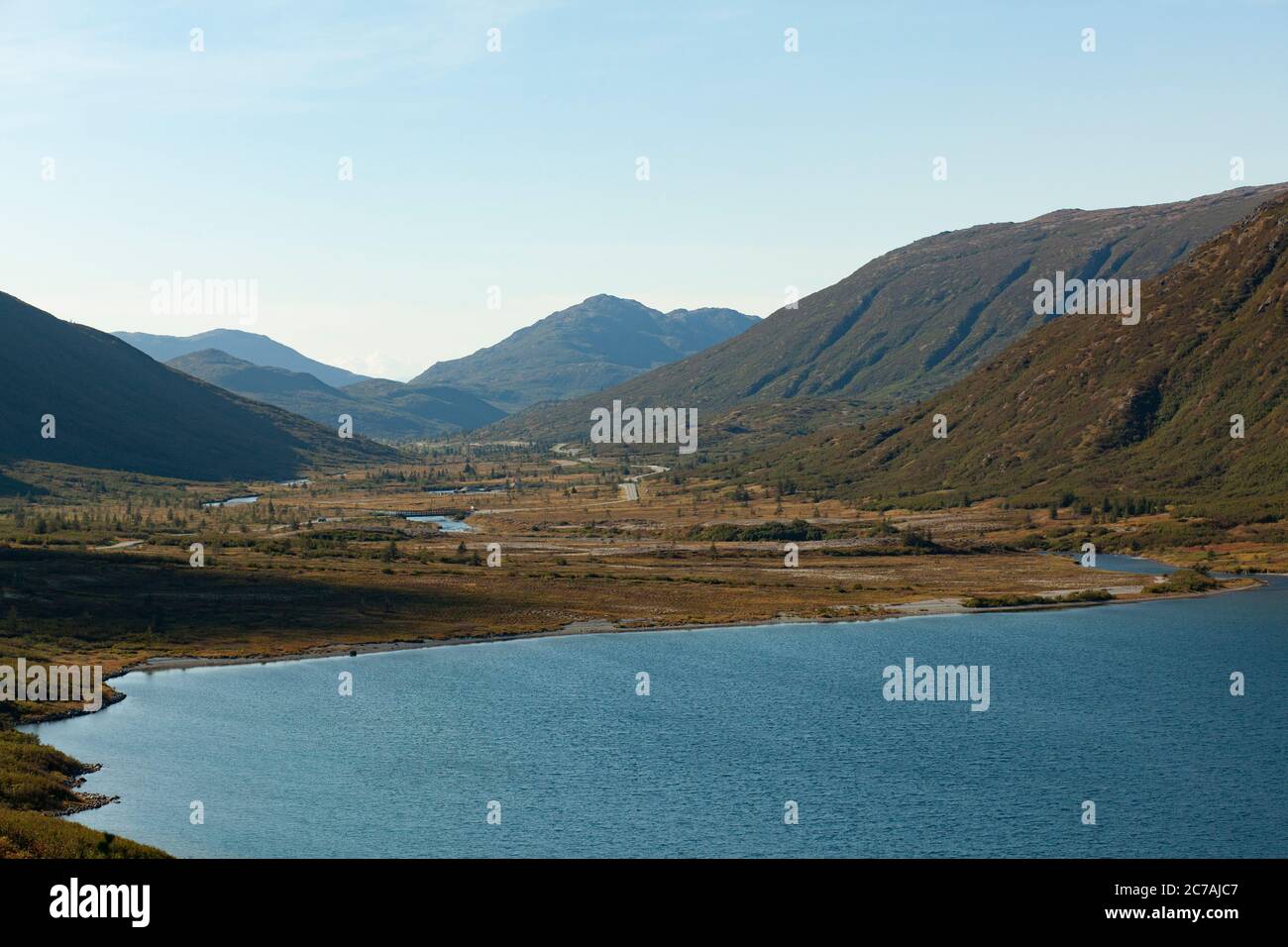 A serene valley in Alaska with a calm lake nestled between rugged ...
