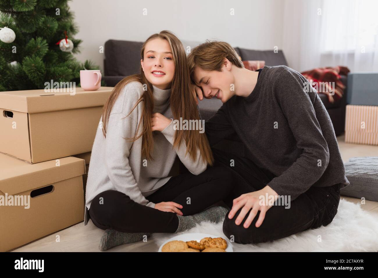 Portrait of beautiful girl sitting on floor with boy that leaning his ...