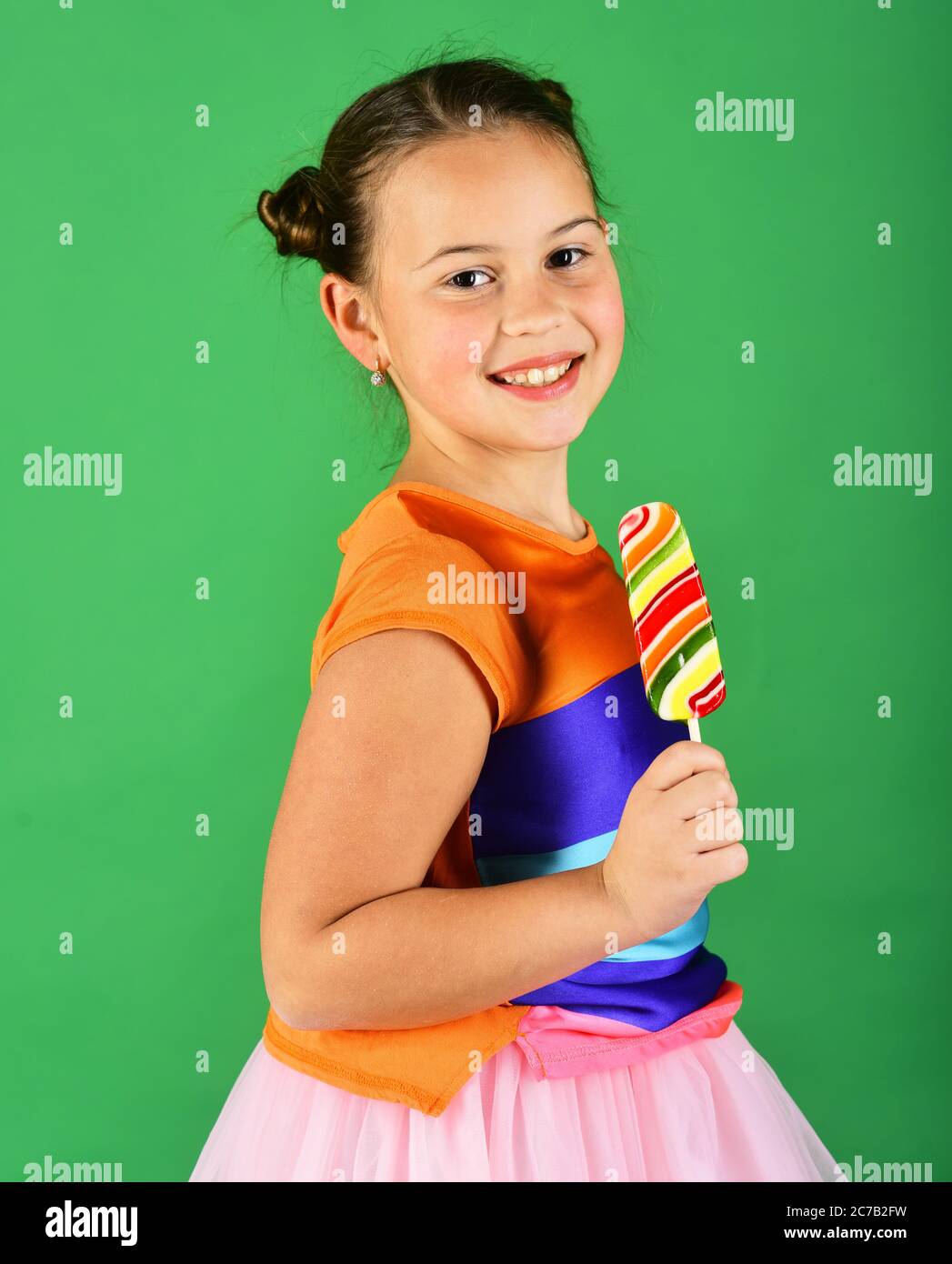 Child with happy face poses with candy on green background. Girl eats ...