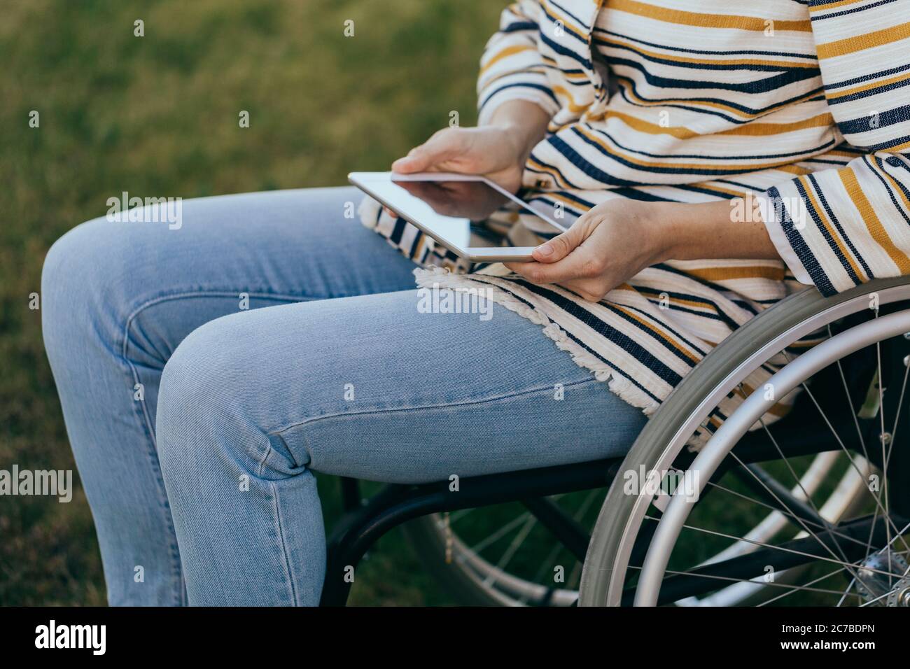 Fashionably dressed woman in a wheelchair with a modern tablet in hand ...