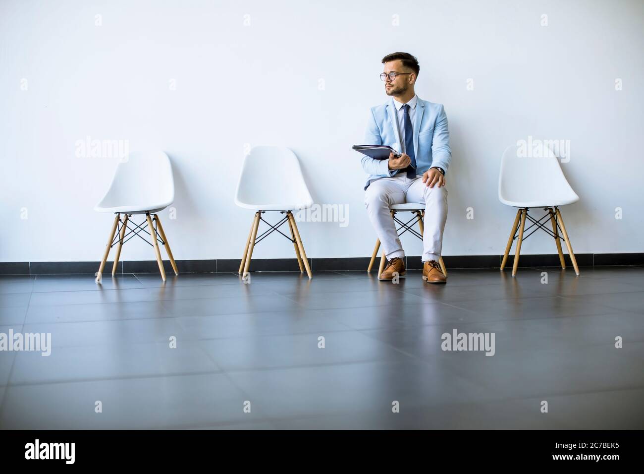 Young man sitting at chair in the waiting room with a folder in hand ...