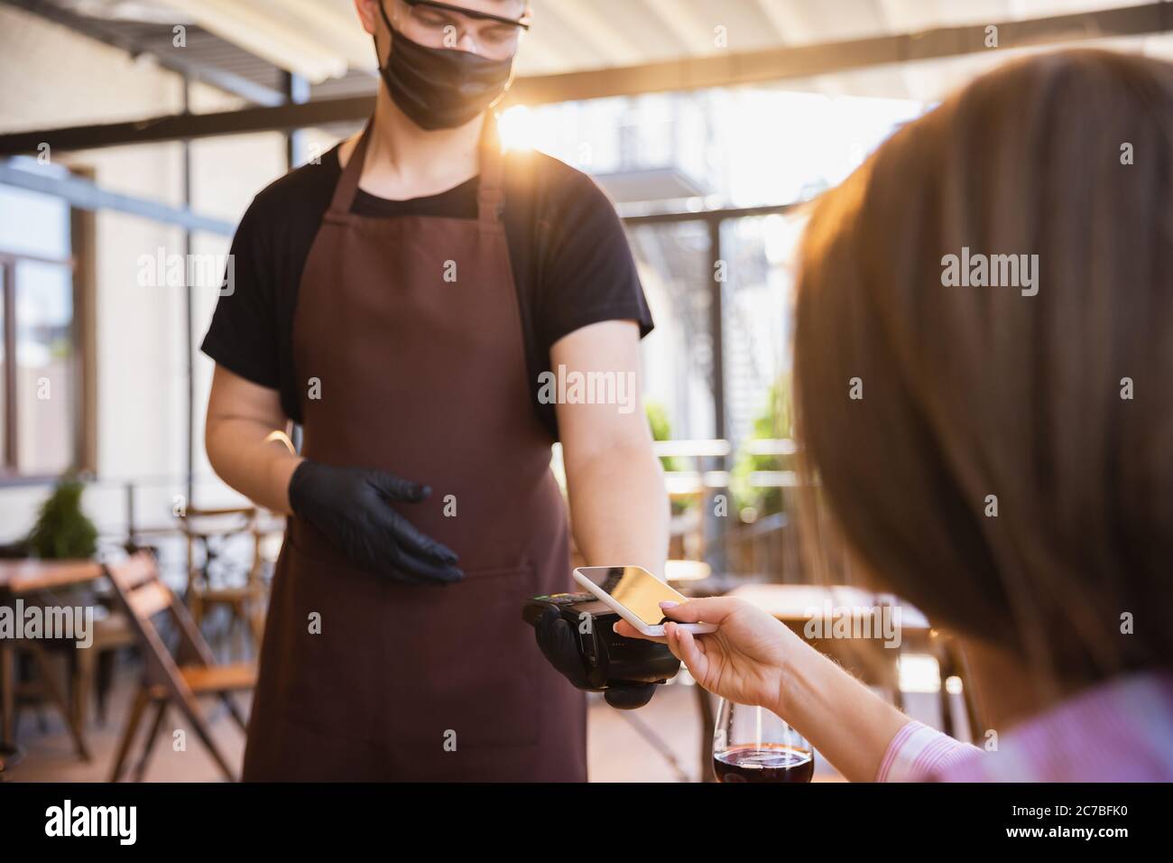 The waiter works in a restaurant in a medical mask, gloves during ...
