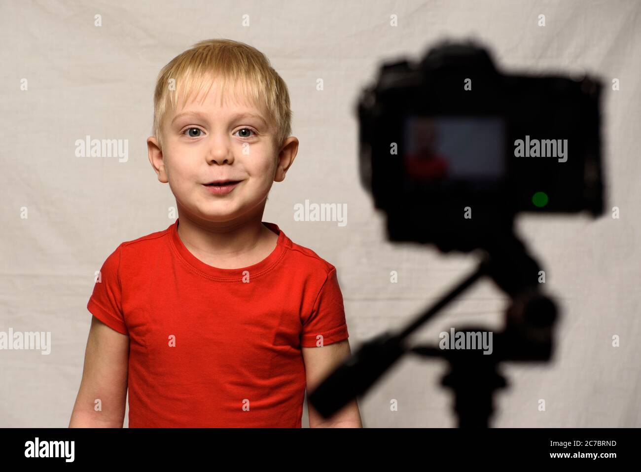 Smiling blond boy in front of the camera lens. Little video blogger ...