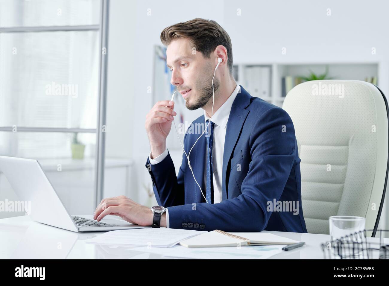 Busy young manager with stubble sitting at desk and talking through ...