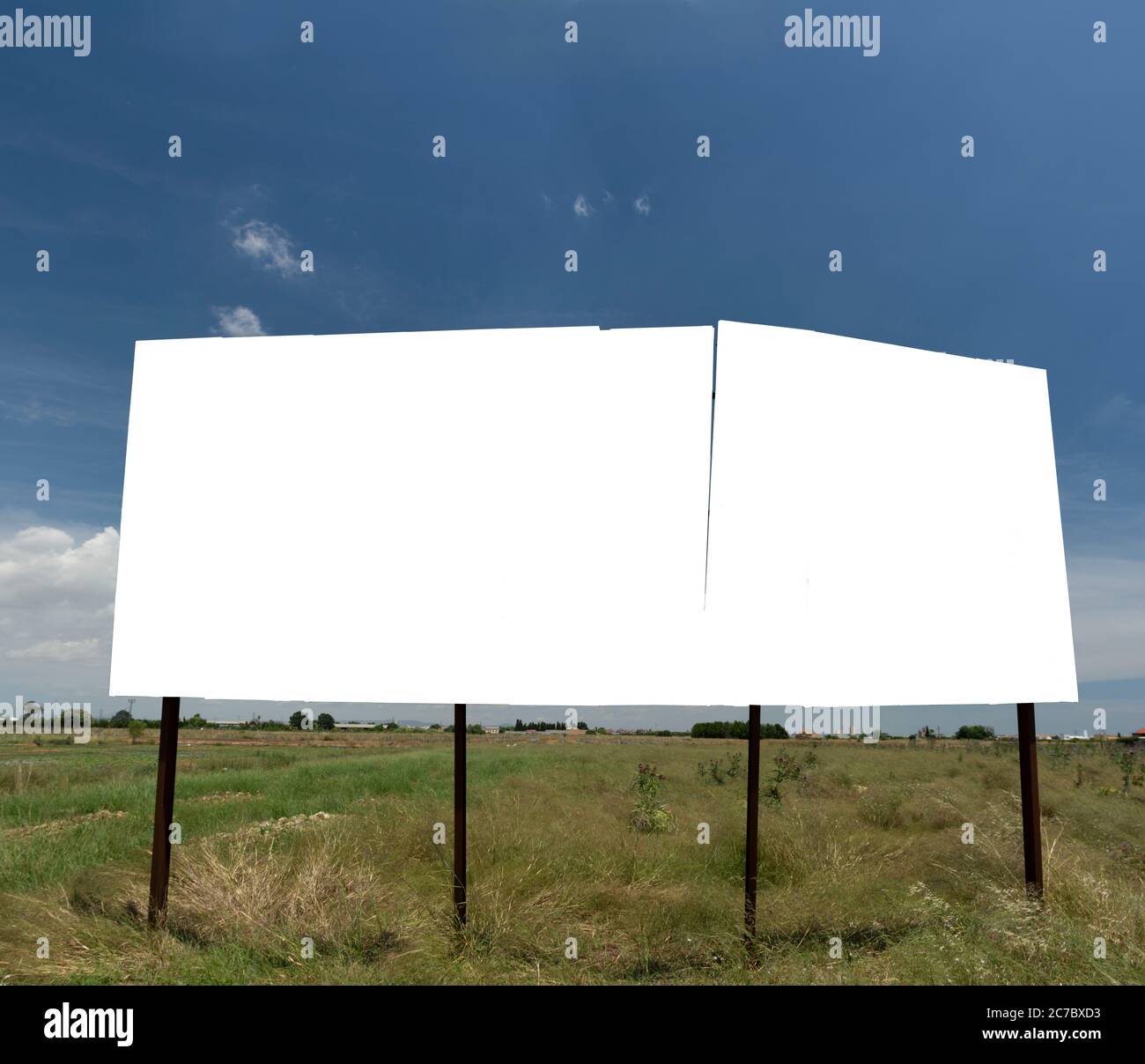 One old multi panel billboard next to a road in the field and blue sky ...