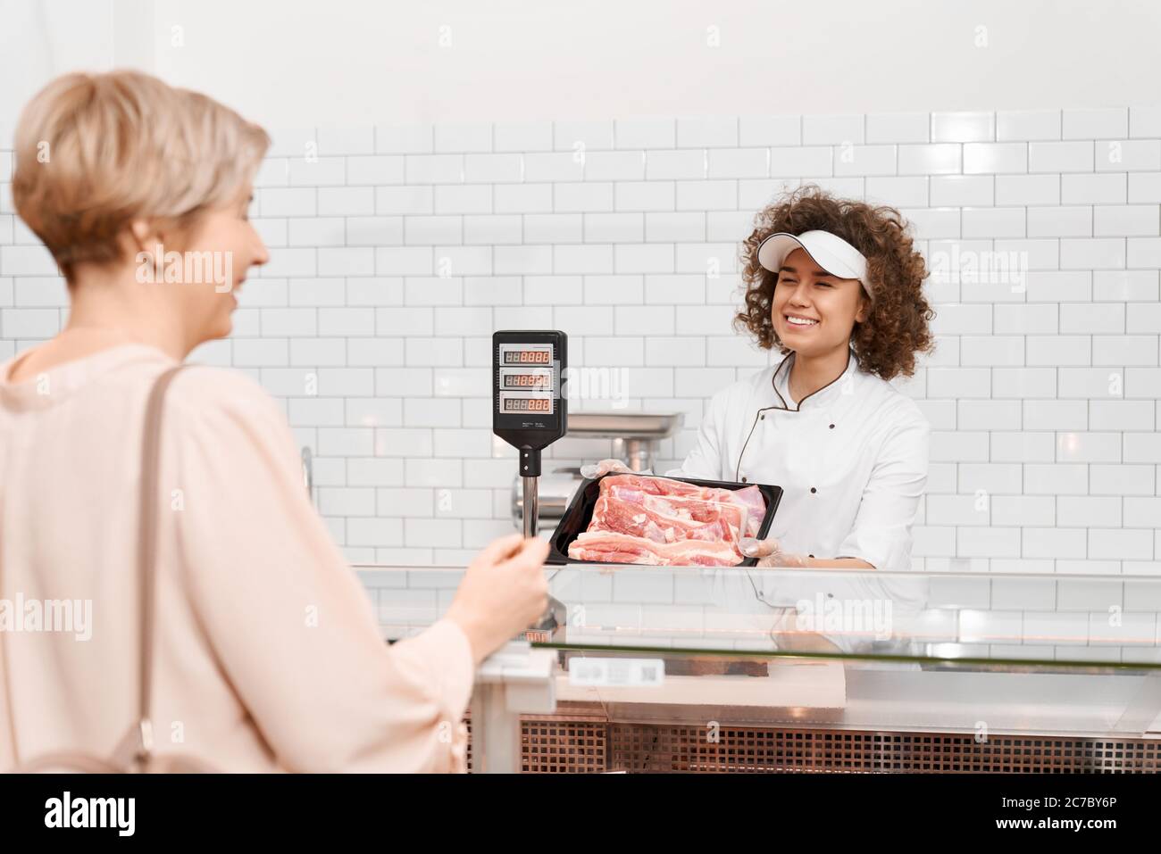 Young smiling woman with curly hair demonstrating to lady raw pork ...