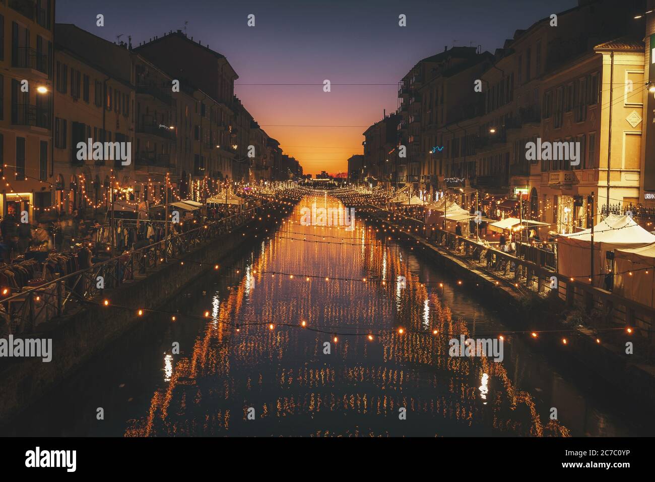 Reflective shot of string lights above river between the buildings ...