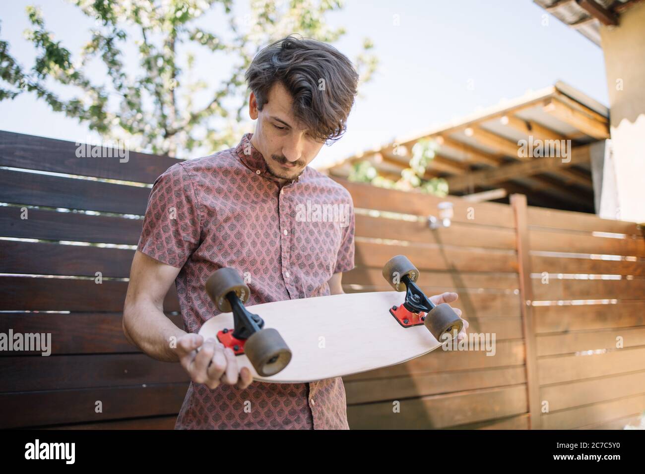 Brunette man holding skateboard and checking wheels Stock Photo - Alamy