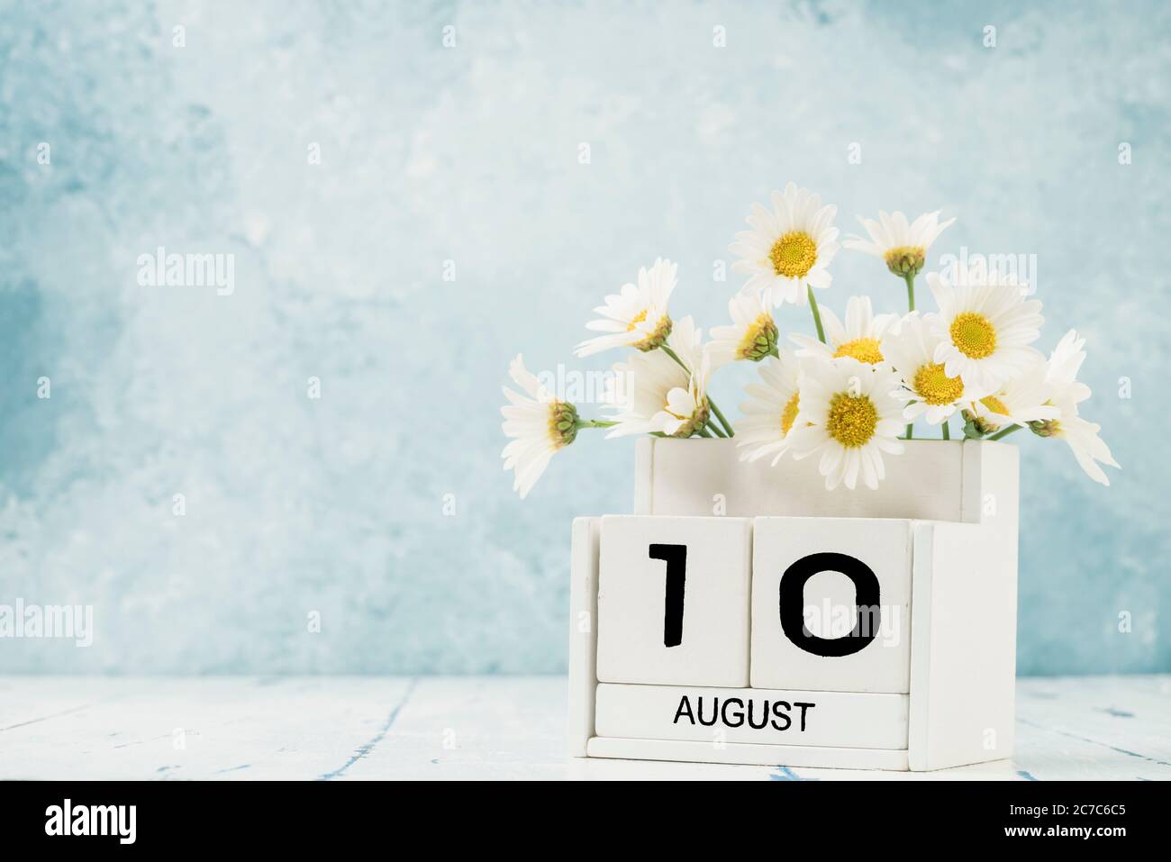 White cube calendar for august decorated with daisy flowers over blue ...