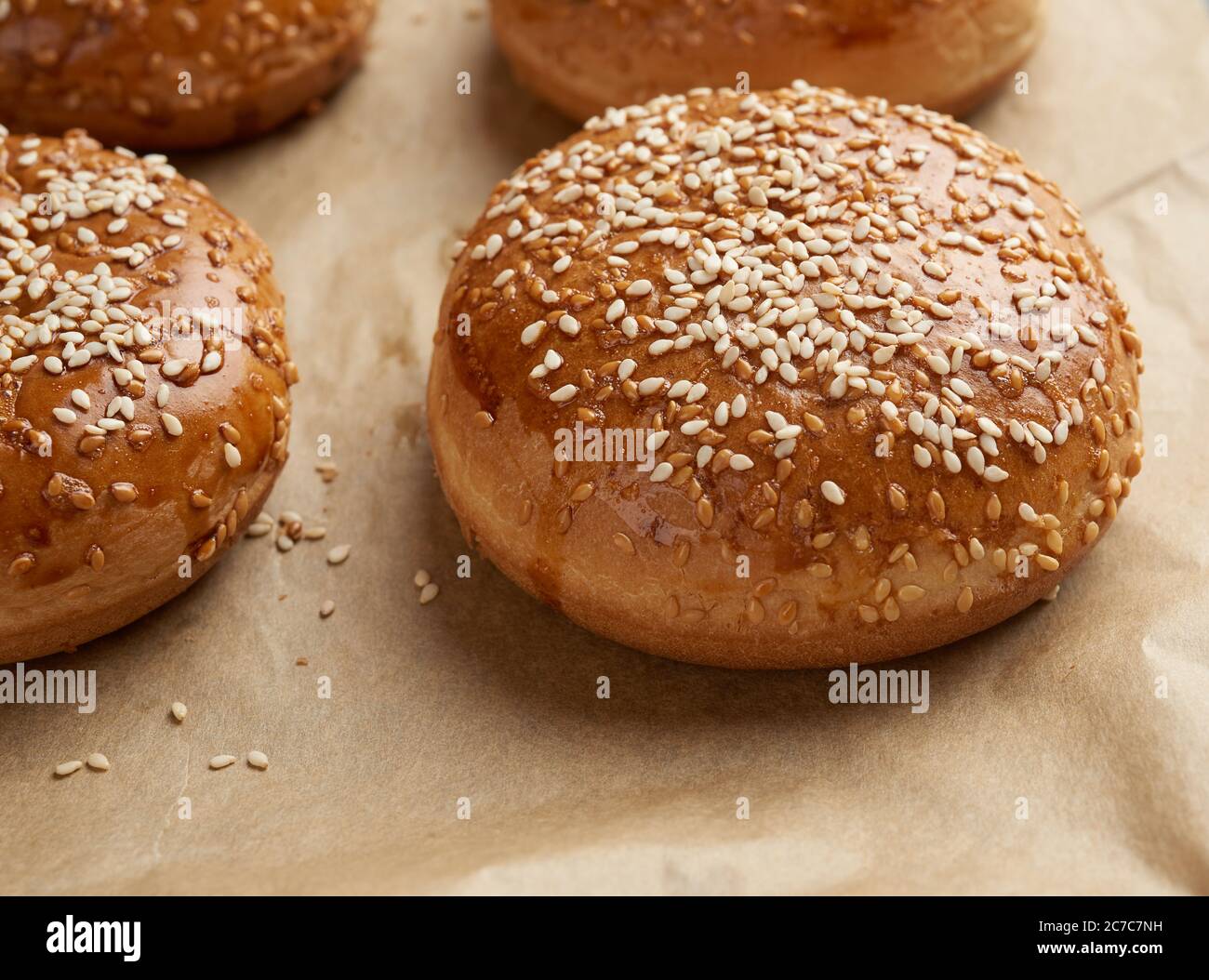 baked sesame buns on brown parchment paper, ingredient for a hamburger ...