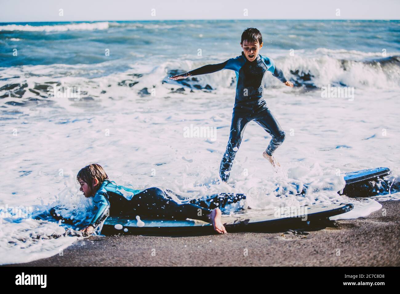 kids enjoying a funny surf day in the shore of a sunny beach in their ...