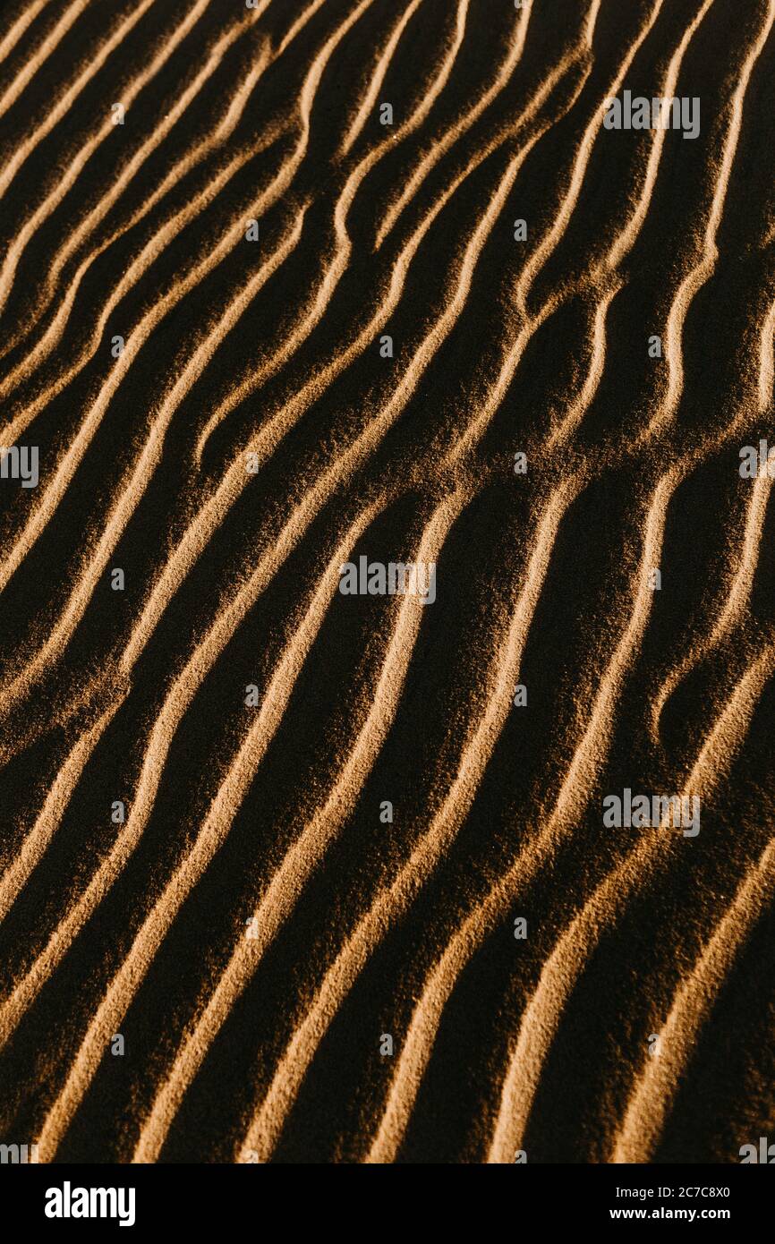Vertical overhead shot of the wavy sand with the sun shining on it ...