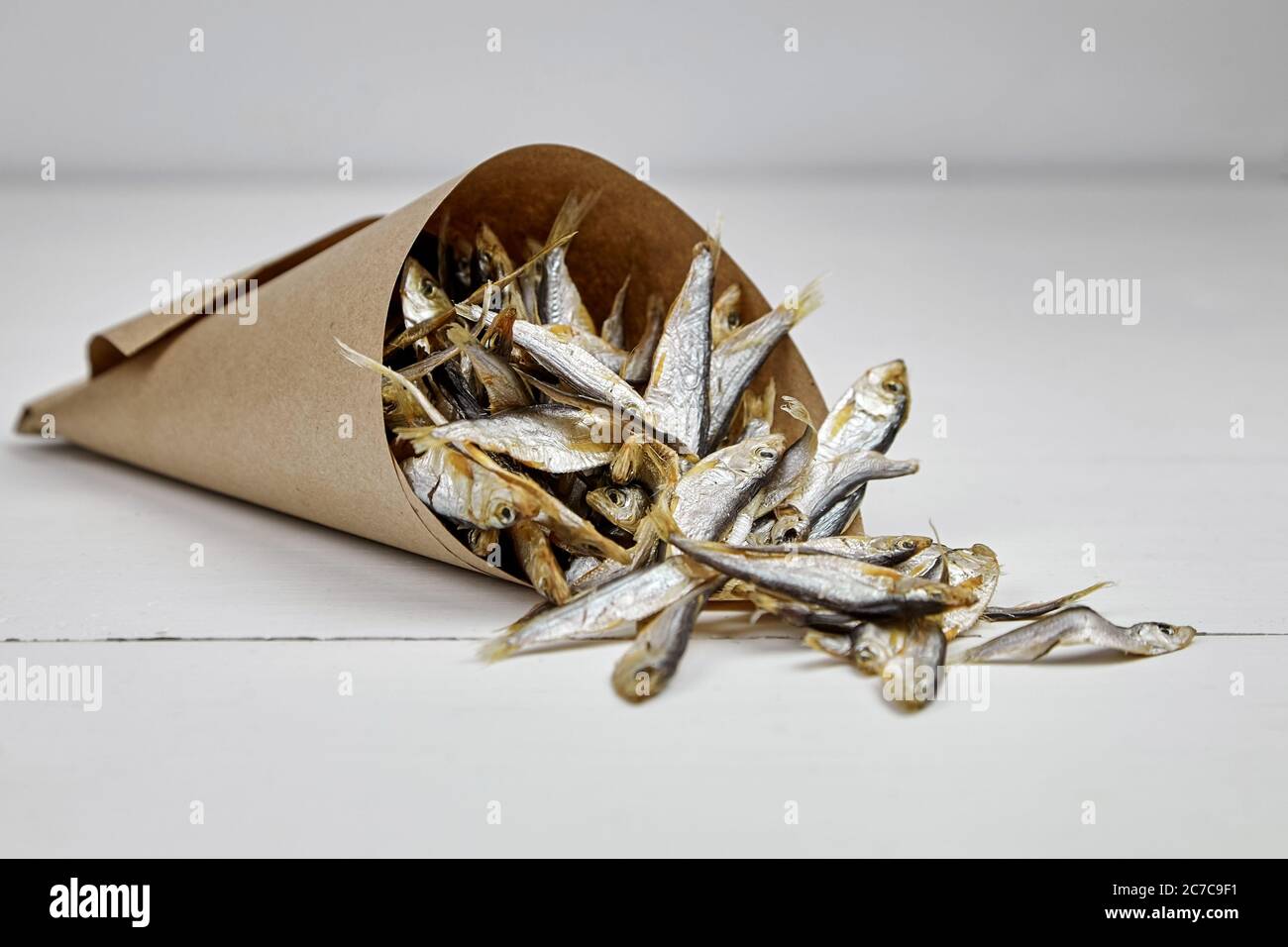 Dried small salted sprat or kilka fish in paper bag on white wooden ...