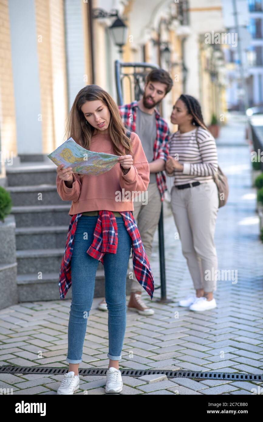 Girl looking with map, boyfriend with girlfriend talking behind Stock ...