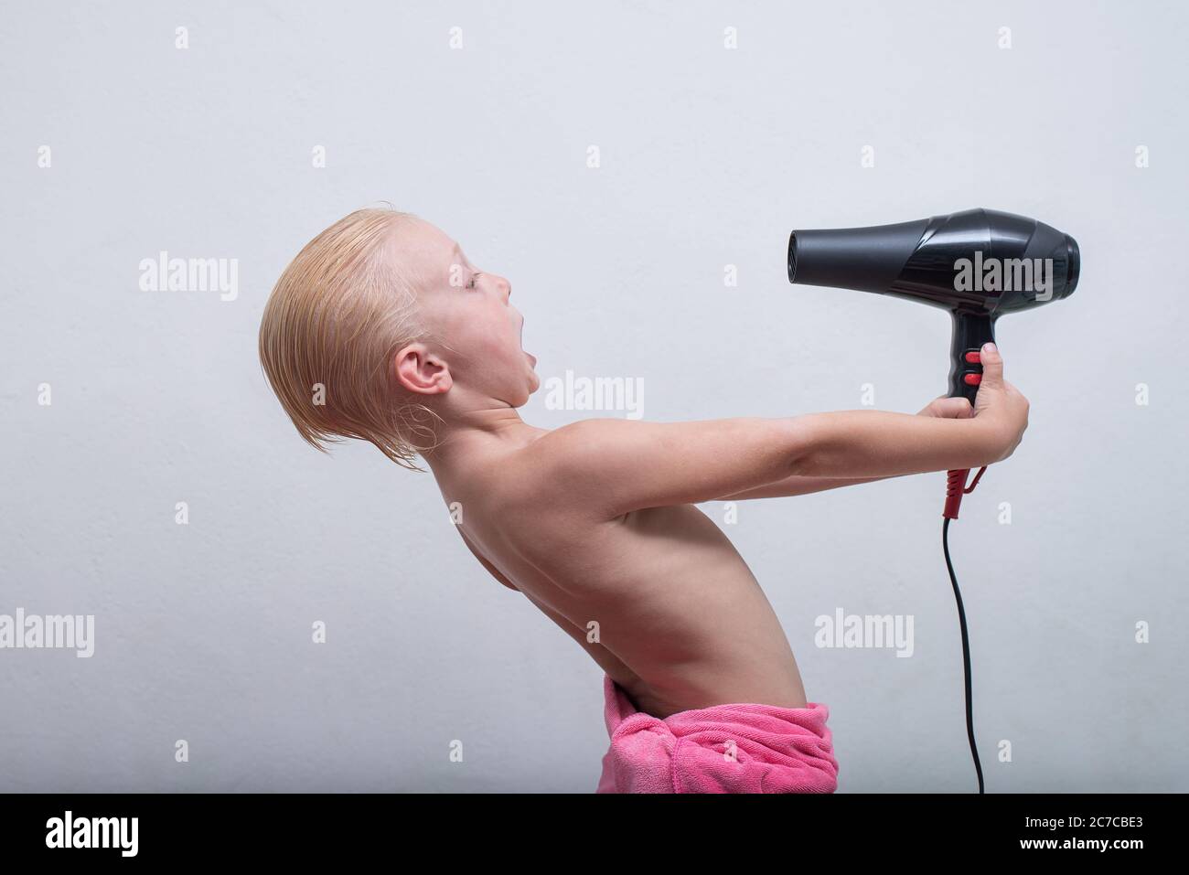 Blond boy with wet hair is funny dried by a hairdryer. White background ...
