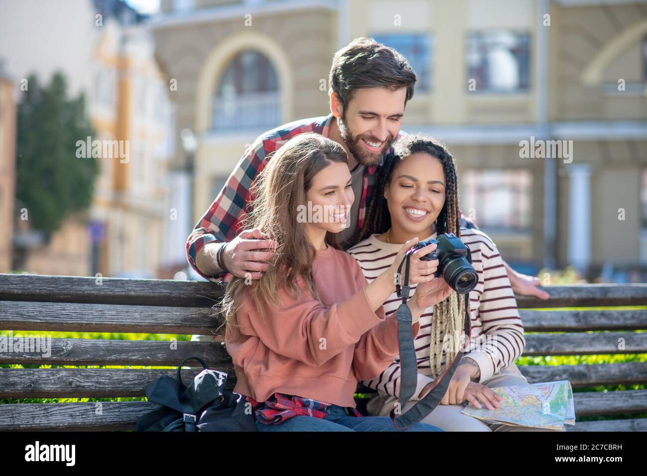 Guy is standing two girls sitting with camera in hands Stock Photo - Alamy