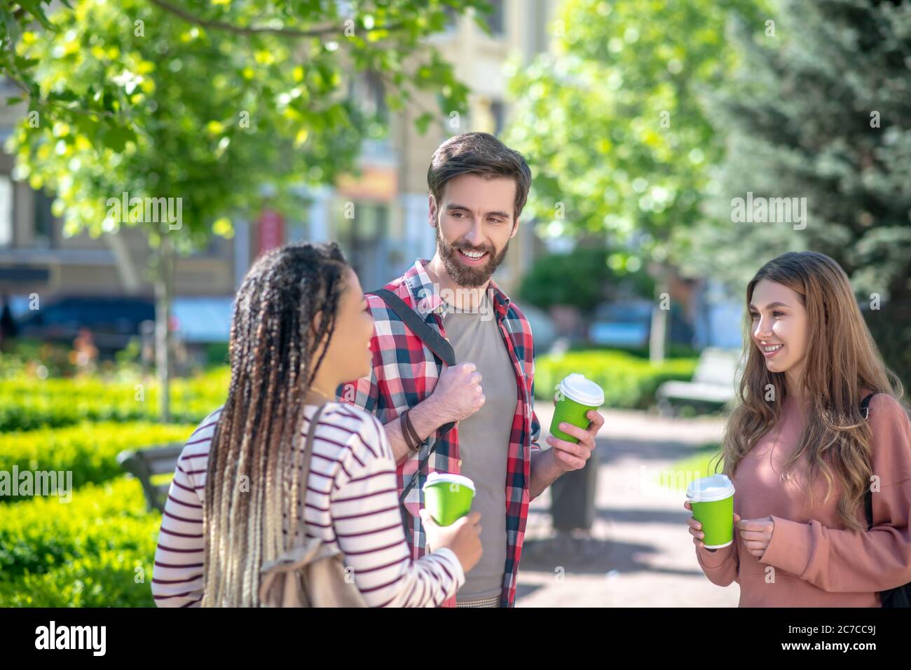 Three friends chatting drinking coffee while standing in park Stock ...