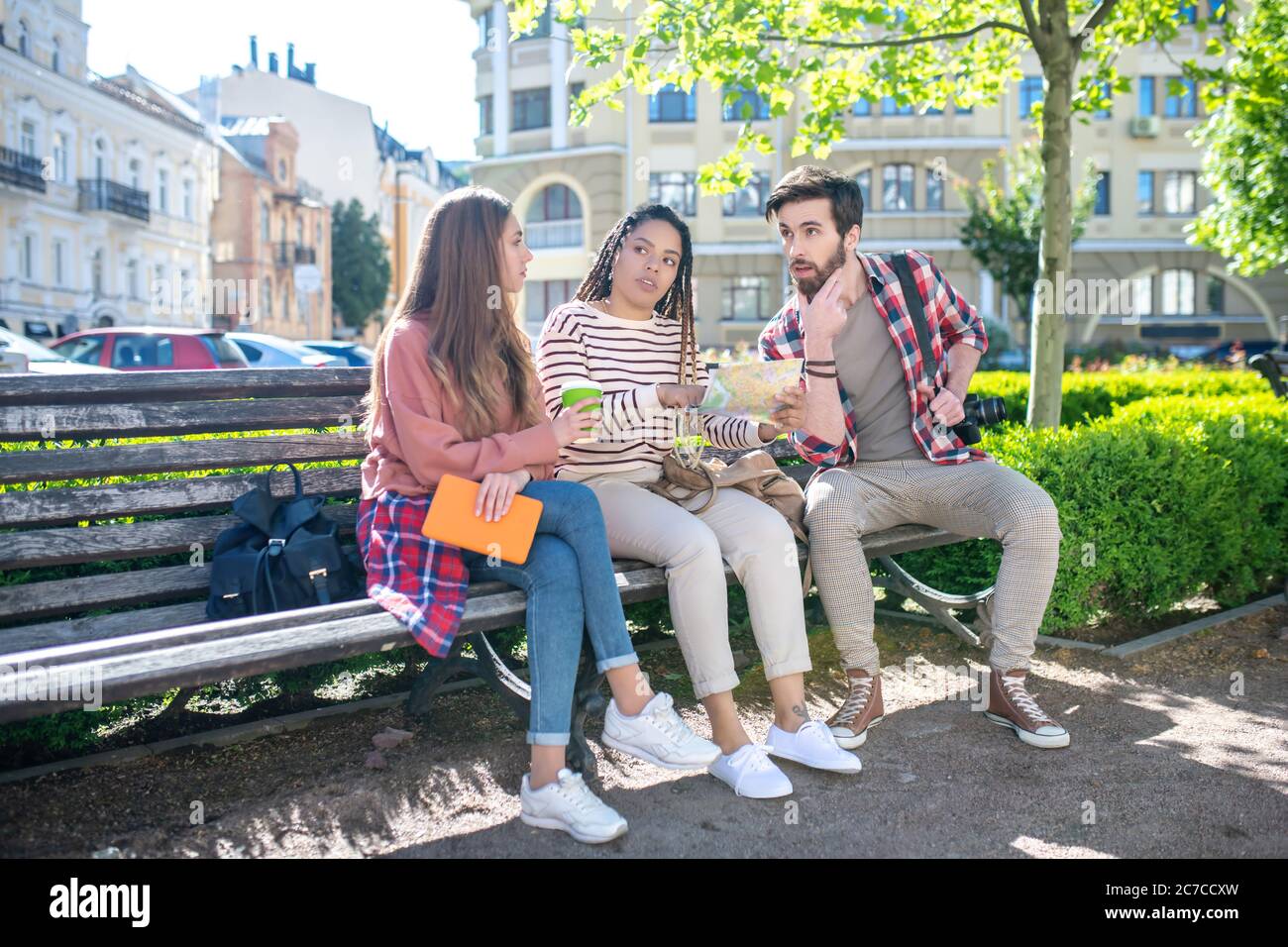 Discussing guy and two girls with tablet and map on bench Stock Photo ...