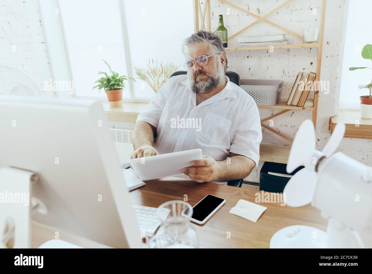Upset. Businessman, manager in office with computer and fan cooling off ...