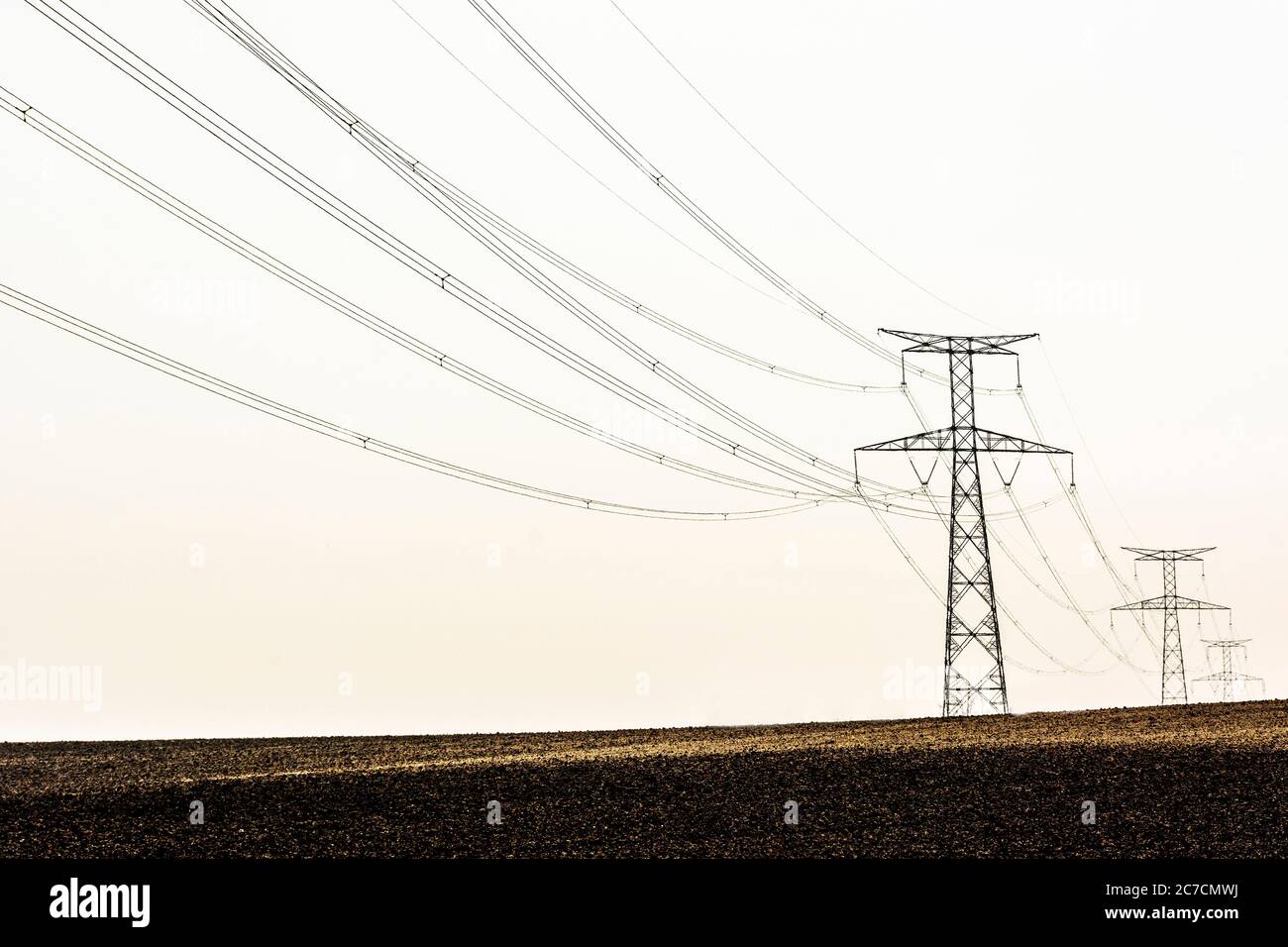 Power lines stretch across an open field under a clear sky during late ...