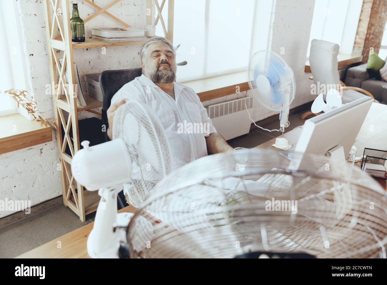 More fans. Businessman, manager in office with computer and fan cooling ...