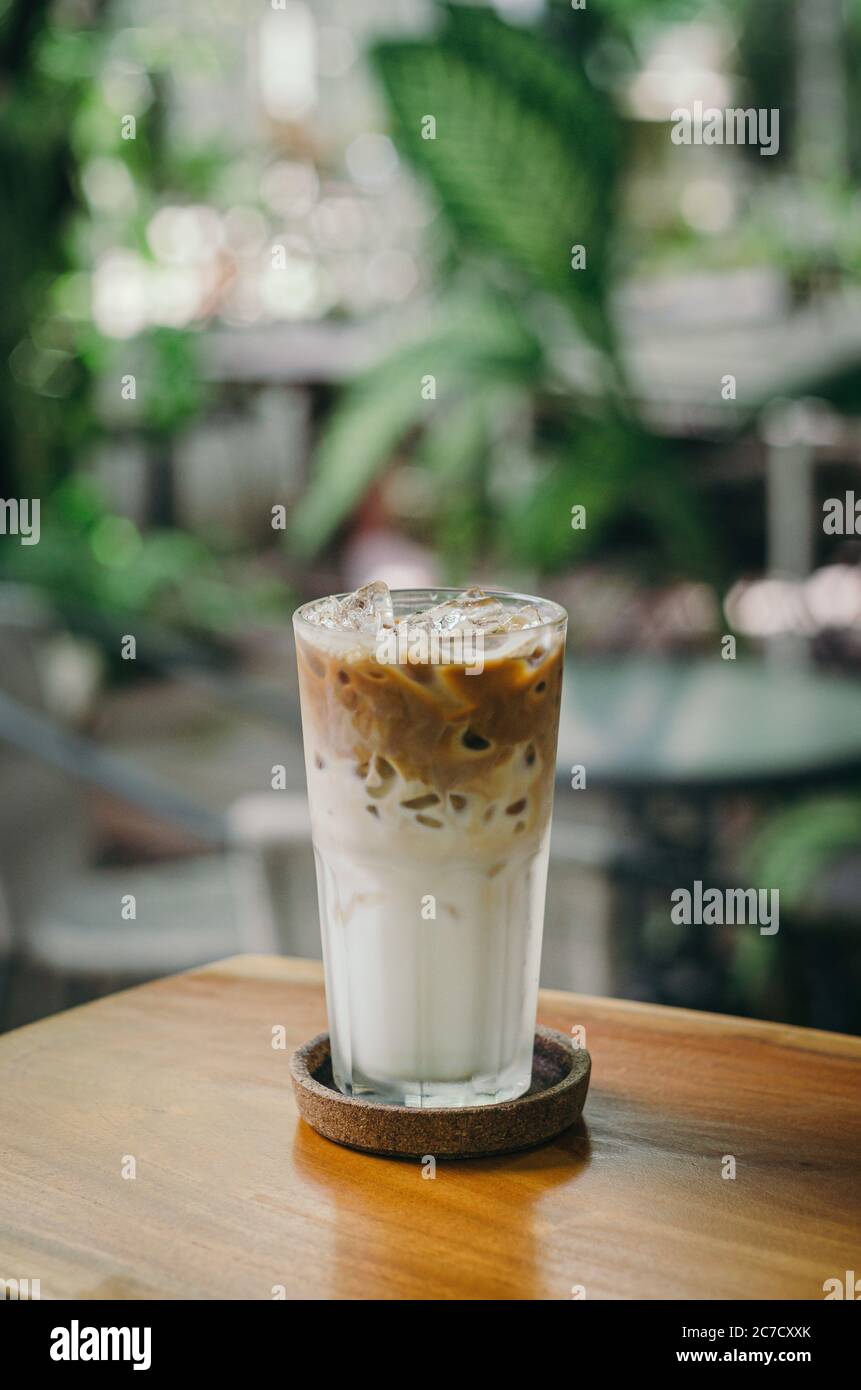 Vertical shot of a latte with ice on a wooden surface and a blurred ...