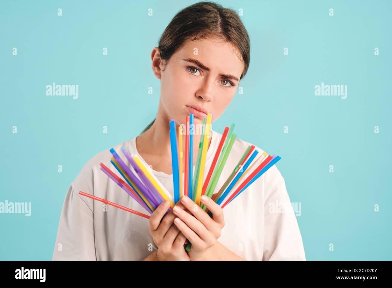 Upset girl holding plastic straws in hands sadly looking in camera over ...