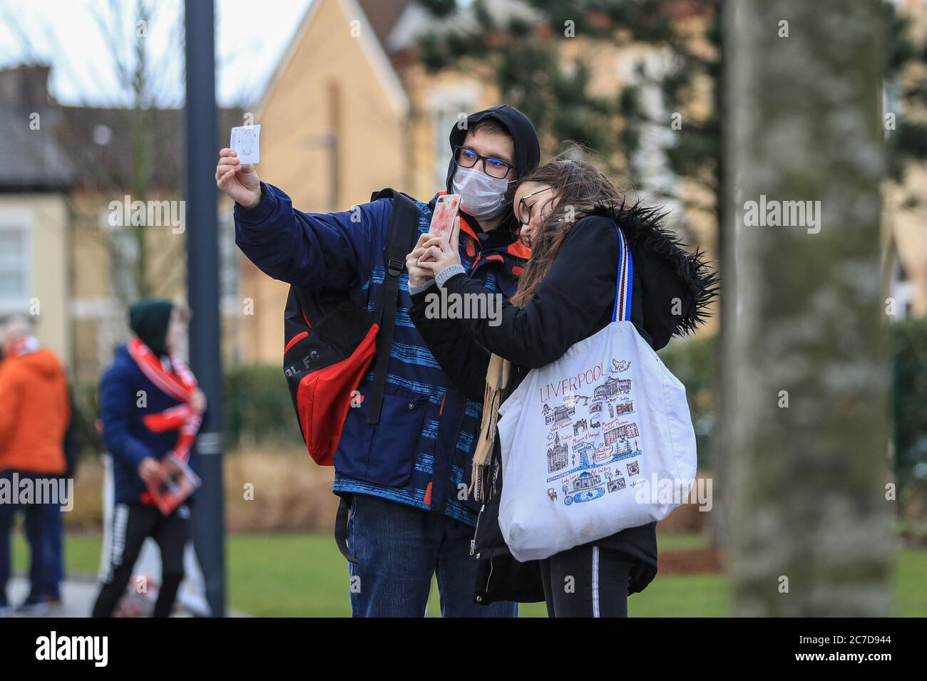 Two Liverpool fans take selfies while one wears a mask outside Anfield ...
