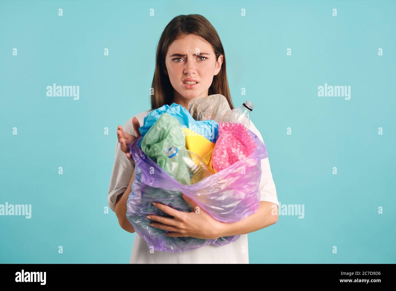Upset girl holding plastic waste depressedly looking in camera over ...