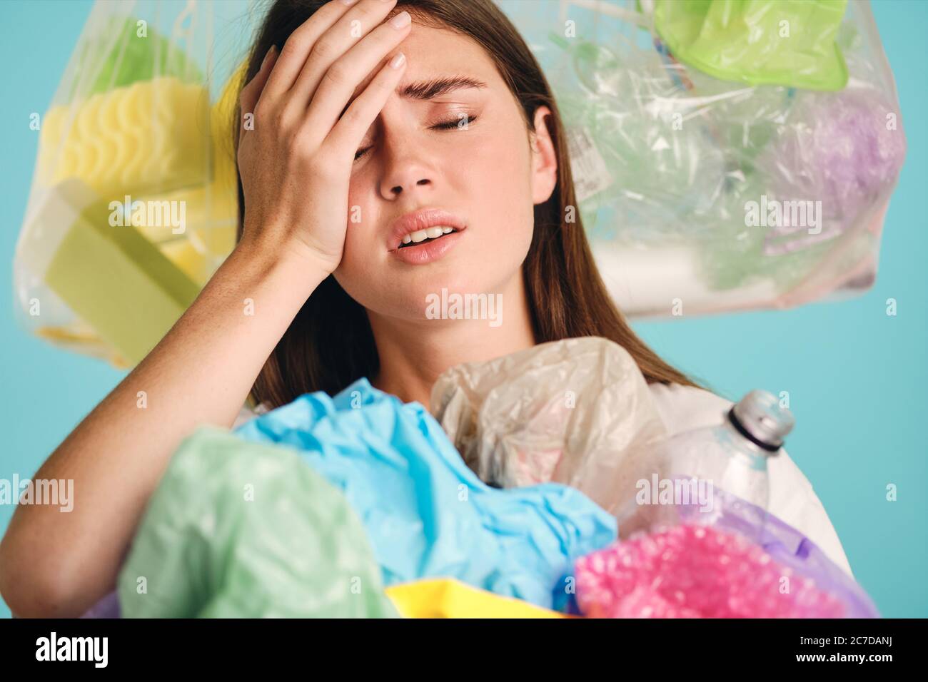 Close up tired upset girl with plastic waste around over colorful ...