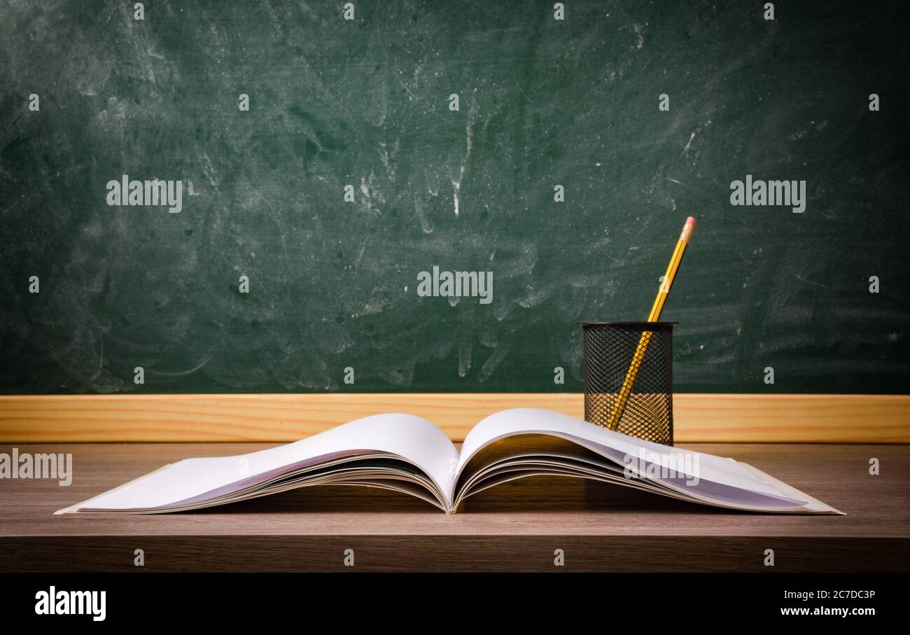 Book and pen with pencil and scissors on school desk with blackboard in ...