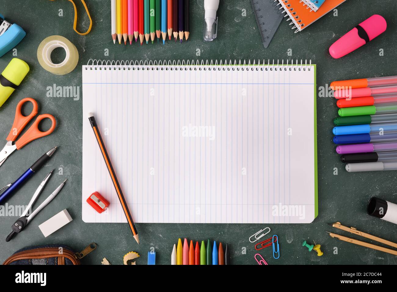 Open notebook with sheet of lines and school supplies around on green ...