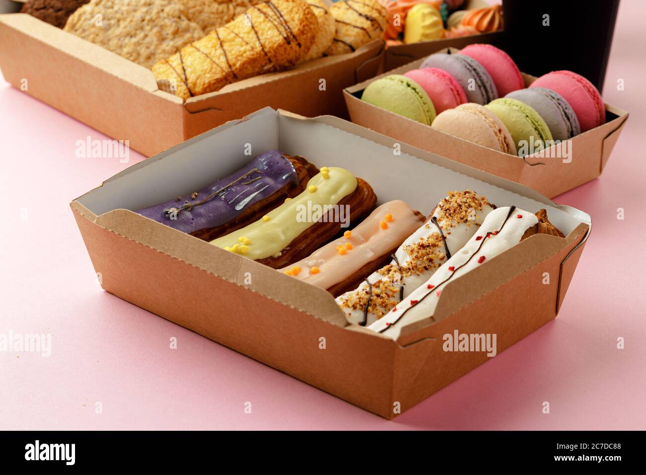 Carton boxes with eclair cakes and cookies on pink surface Stock Photo ...