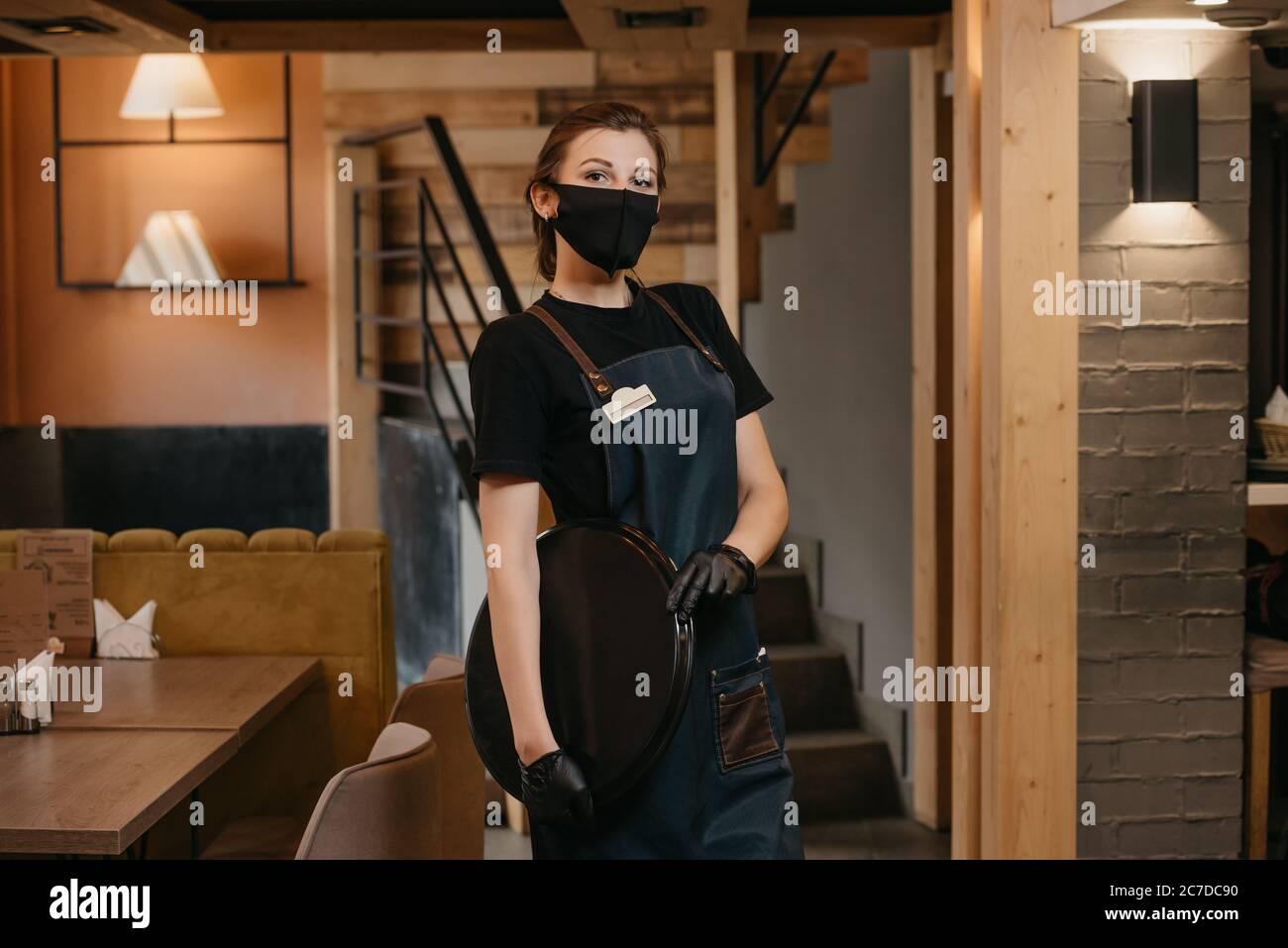 A waitress who wears a medical face mask and black disposable medical ...