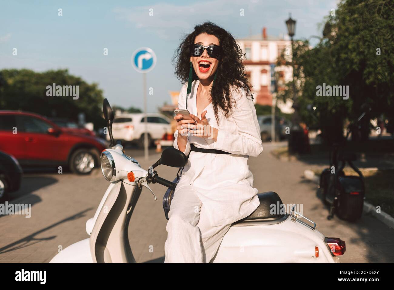 Cheerful lady with dark curly hair in white costume and sunglasses ...