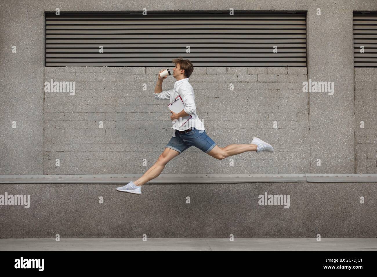 Coffee drinking. Jumping young man in front of city building wall, on ...