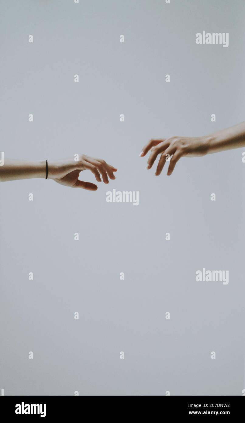 Vertical shot of two hands reaching for one another on a gray ...