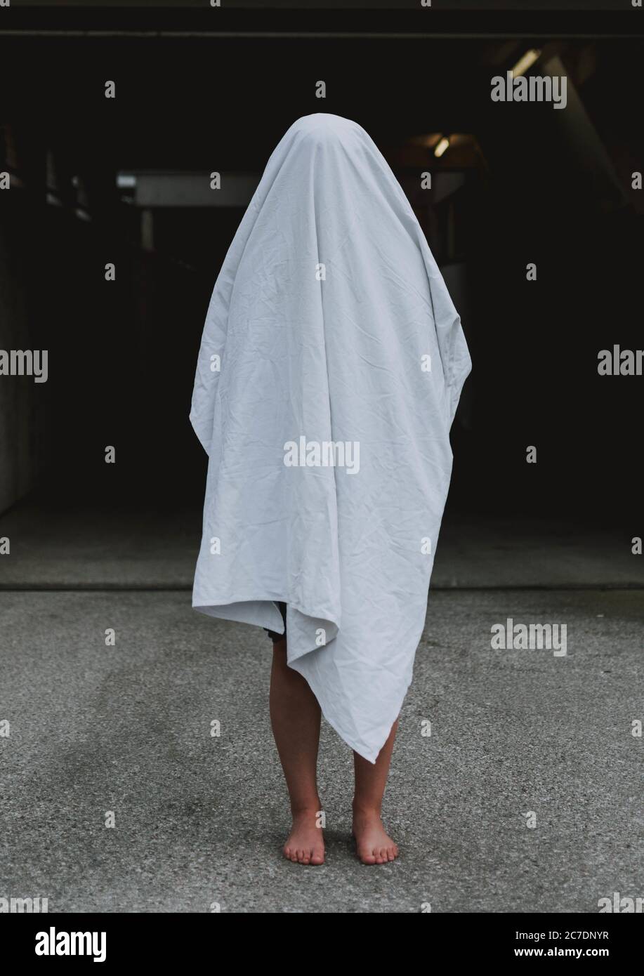 Vertical shot of a barefoot person wearing white ghost sheet.Spooky ...