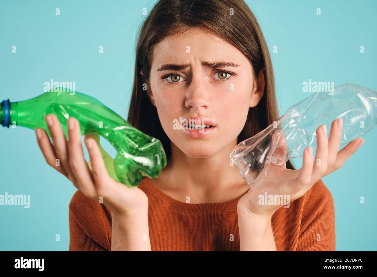 Portrait of upset girl holding empty plastic bottles in hands miserably ...