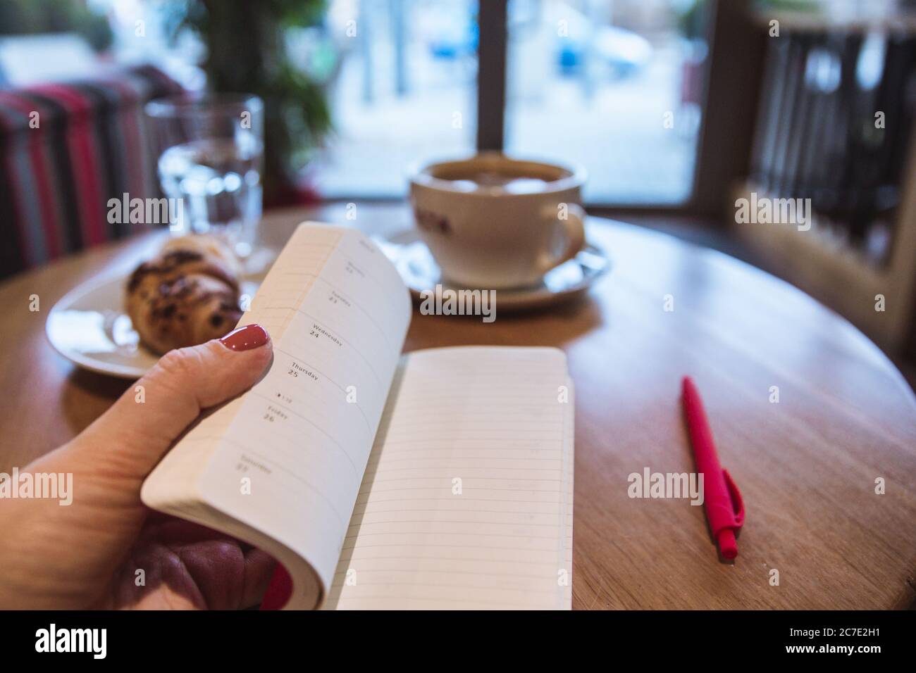 A red note and red pen is on the table in a cafe, a cup of coffee and a ...