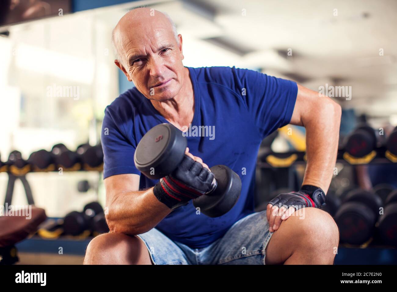 A portrait of bald senior man in the gym training with dumbbells ...