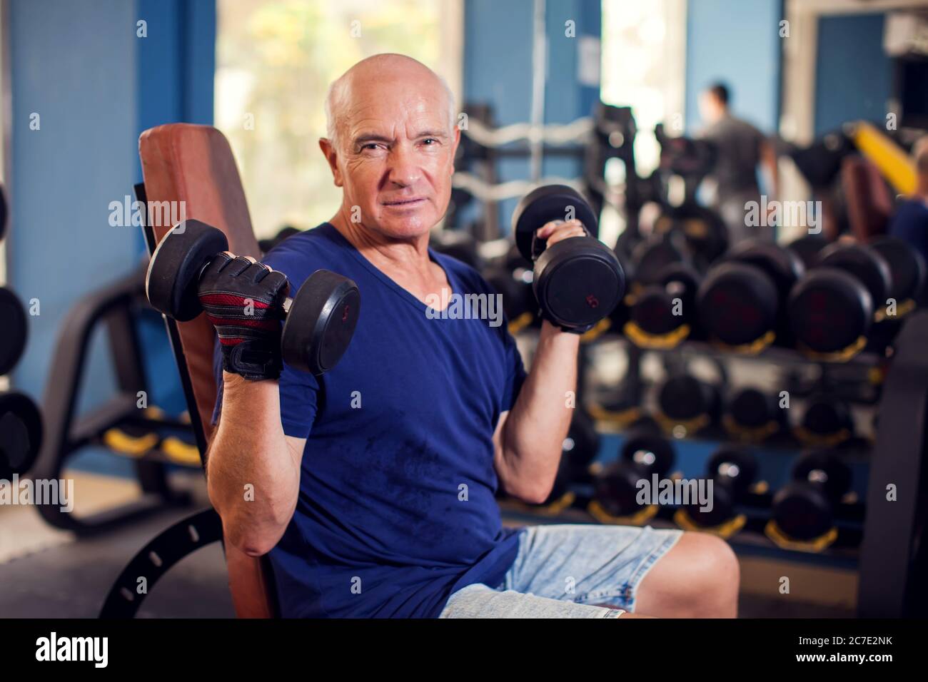 A portrait of bald senior man in the gym training with dumbbells ...