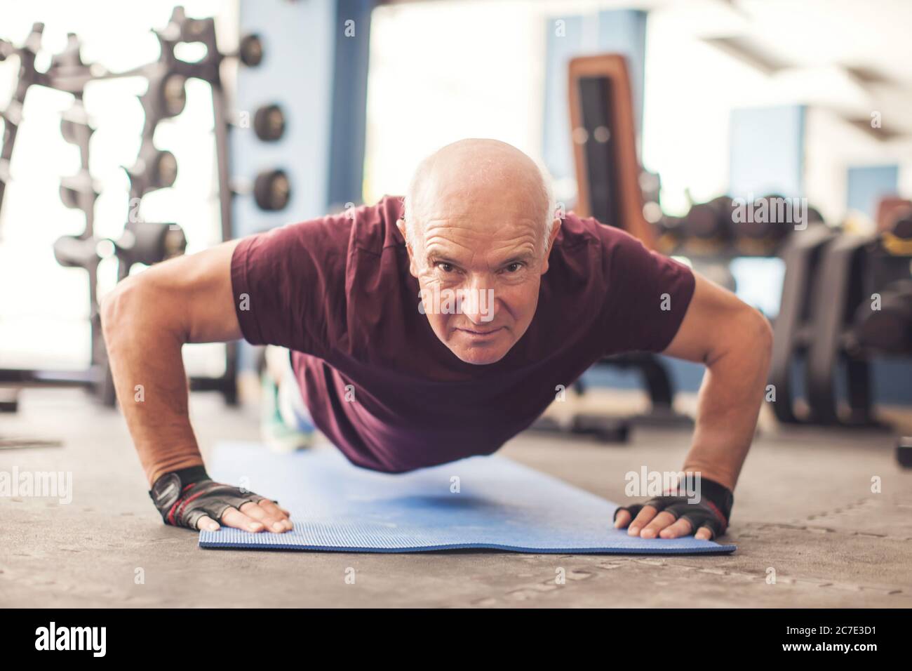 A portrait of bald senior man doing pushups exercise in the gym. People ...